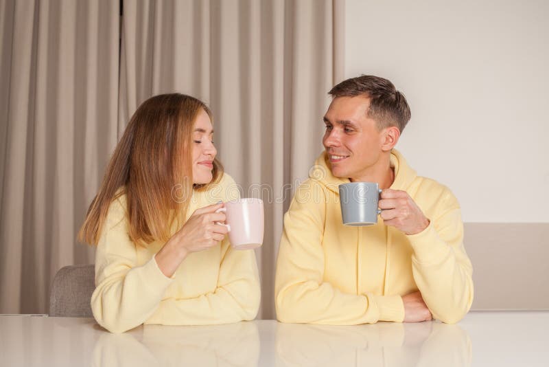 Lovely Couple Drinking Something from the Cups and Sitting by the Table ...