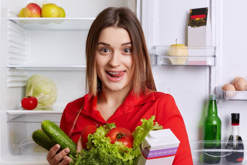 Lovely Young Woman With Happy Look Licks Lips As Sees Much Delcious Food Holds Fresh Cucumbers