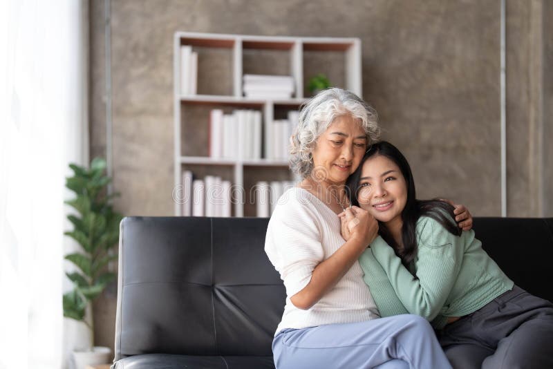 Loving Adult Daughter Hugging Older Mother Standing Behind Couch At