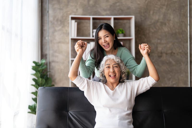 Loving Adult Daughter Hugging Older Mother Standing Behind Couch At