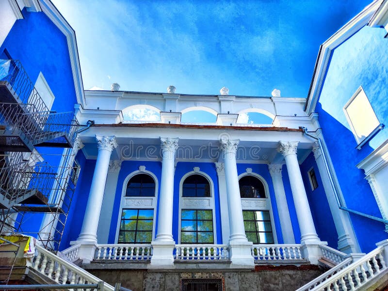 A Low Angle View of a Blue Mansion with White Columns and Balconies ...