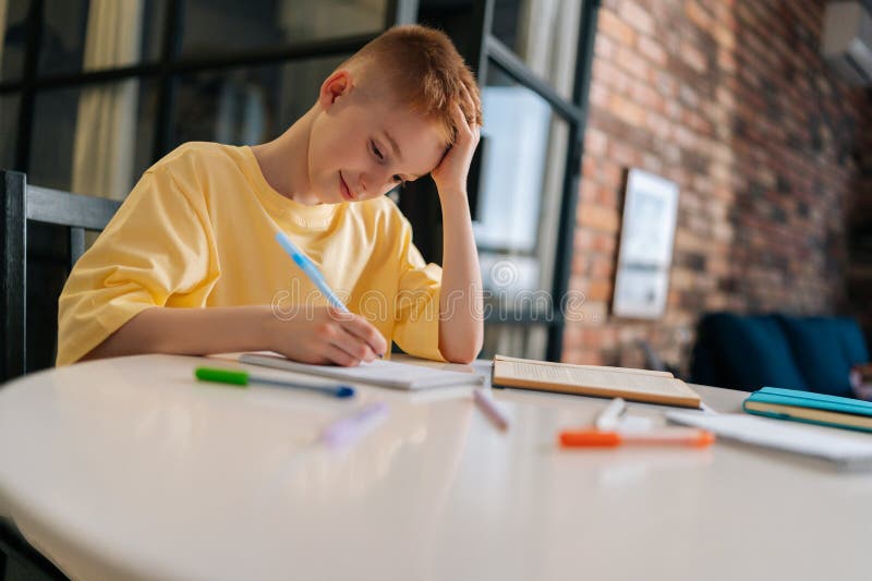 Side View of Focused Schoolboy Studying at Home Doing Homework Sitting at Table Under Light of ...