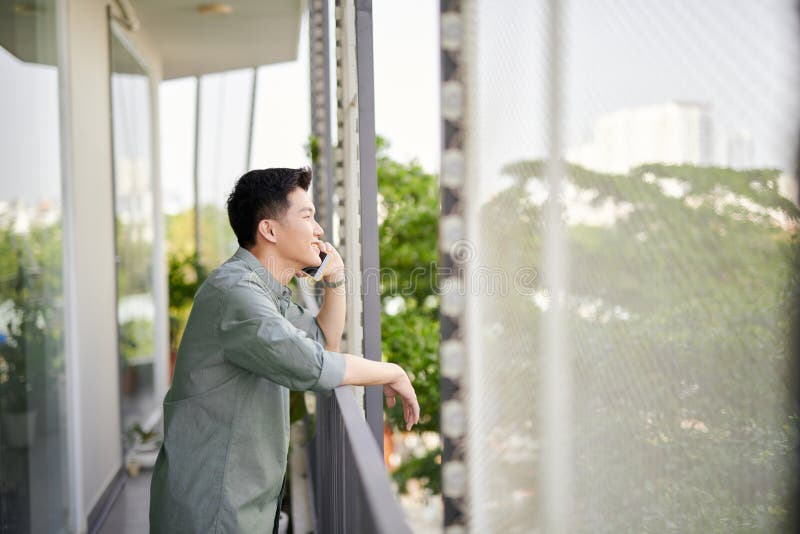 Low-angle View of Smiling Young Man Talking on Mobile Phone, Standing ...