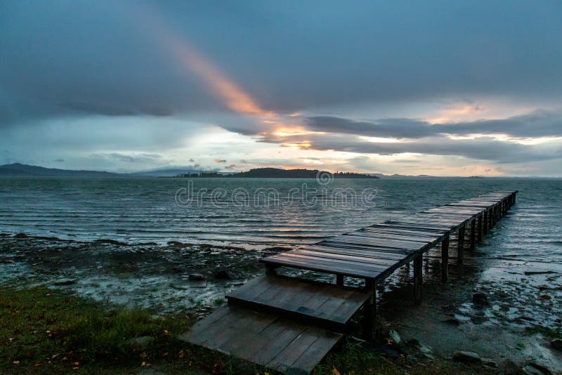 Low Point View of a Pier on a Lake with a Ray of Sun Against a Moody ...