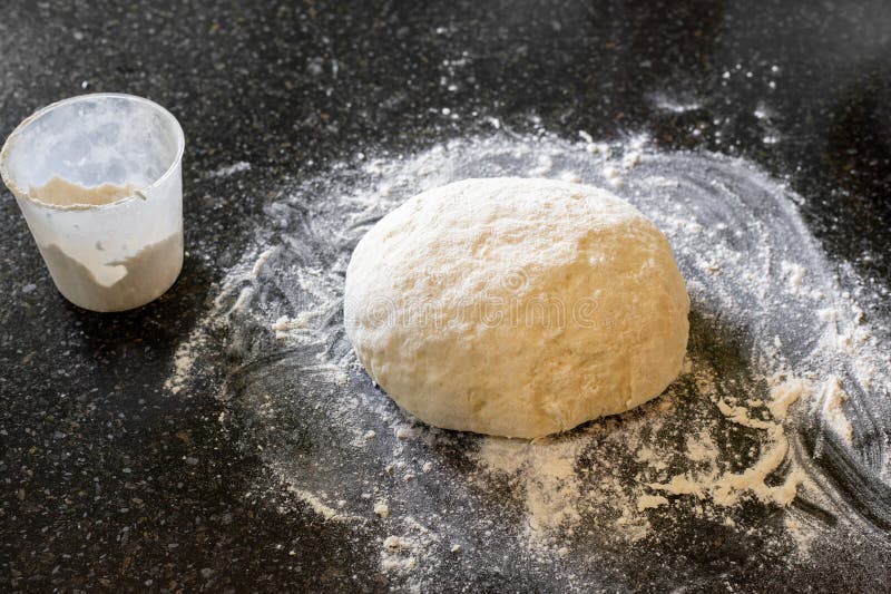 A Lump of Dough on a Black Table with Scattered Flour. Kneaded Dough ...