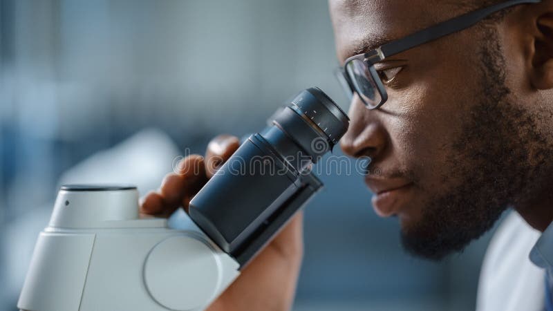 Macro Close Up Shot of a Handsome Black Male Scientist Wearing Glasses and Looking into the ...