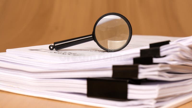 A Magnifying Glass that is Positioned on a Stack of Papers, Which are ...