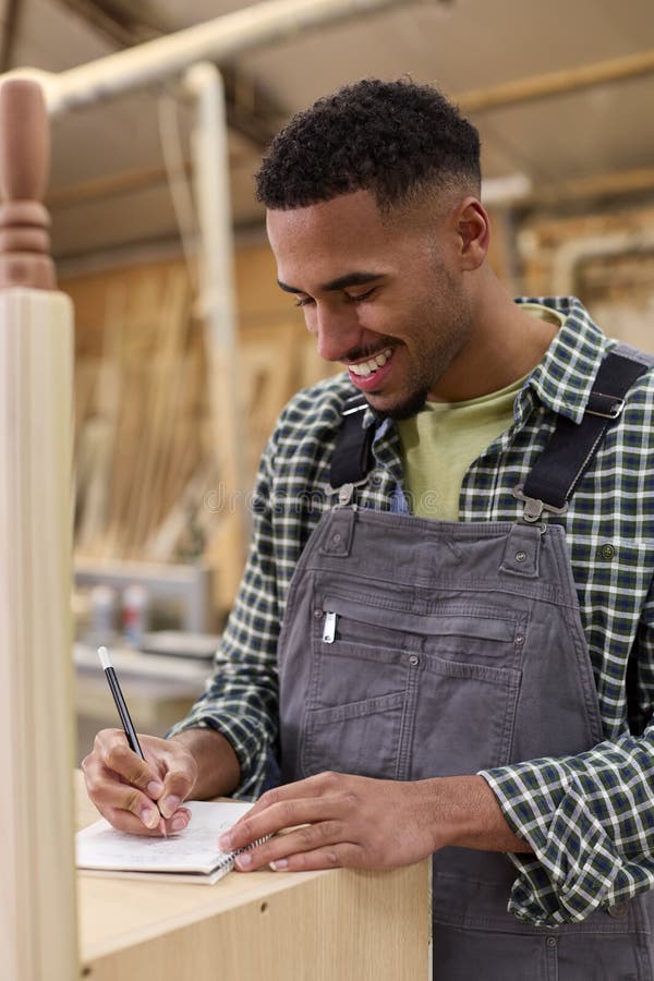 Male Apprentice Working As Carpenter in Furniture Workshop Making Notes ...