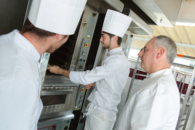 Male Baker and Assistants Using Oven Stock Image - Image of friendship ...
