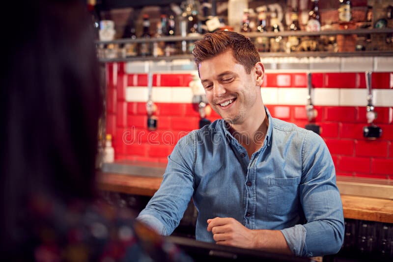 Male Bar Tender Standing Behind Counter Serving Drinks To Customer ...
