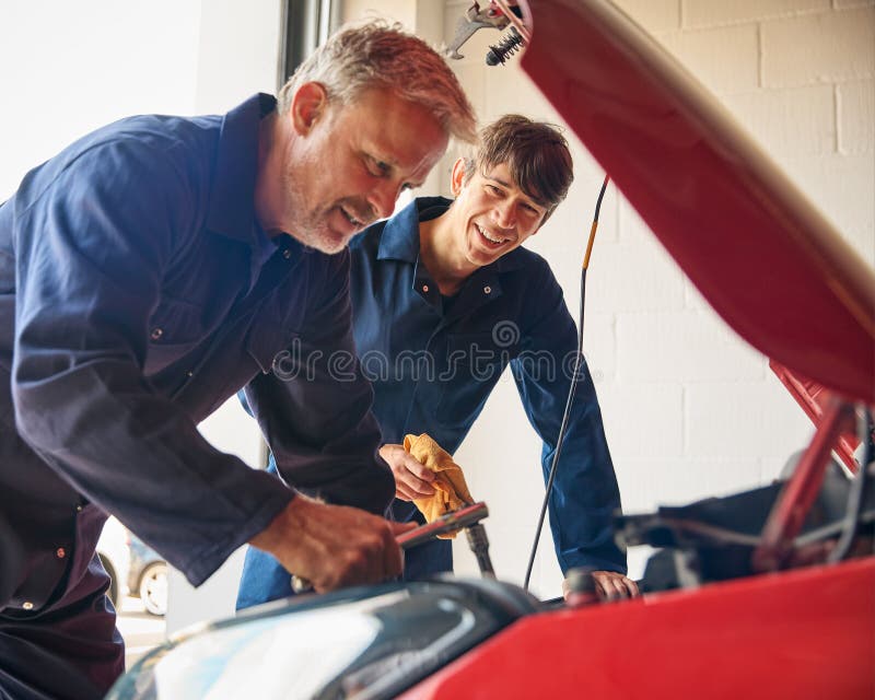 Male Car Auto Mechanic with Trainee Under Bonnet Working on Car Engine ...