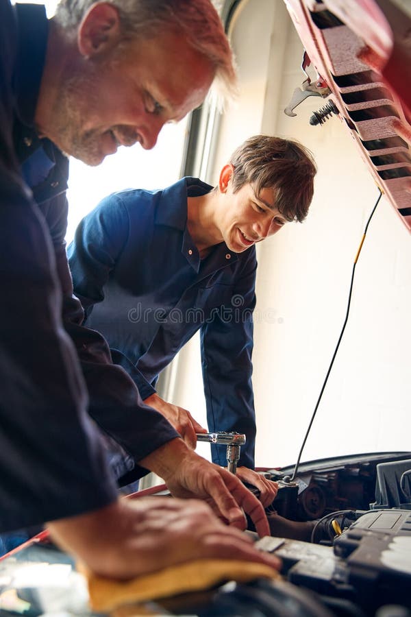 Male Car Auto Mechanic with Trainee Under Bonnet Working on Car Engine ...