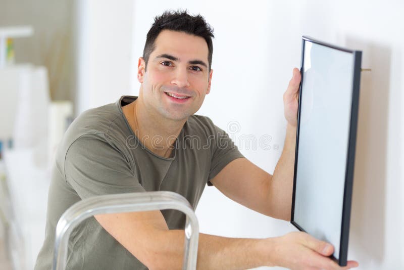 Male Carpenter Hanging Picture Frame on Wall Stock Image - Image of ...