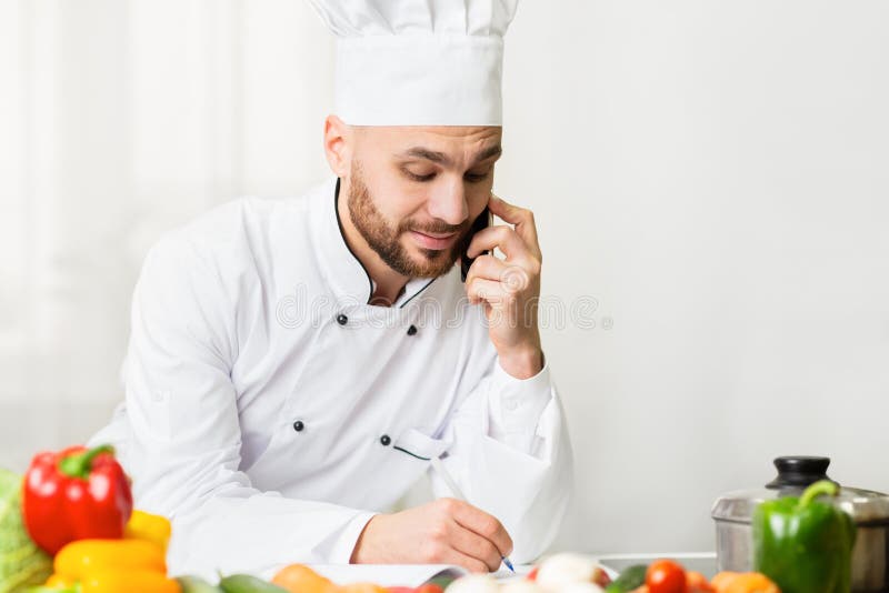 Male Chef Talking on Cellphone Taking Notes Standing in Kitchen Stock ...