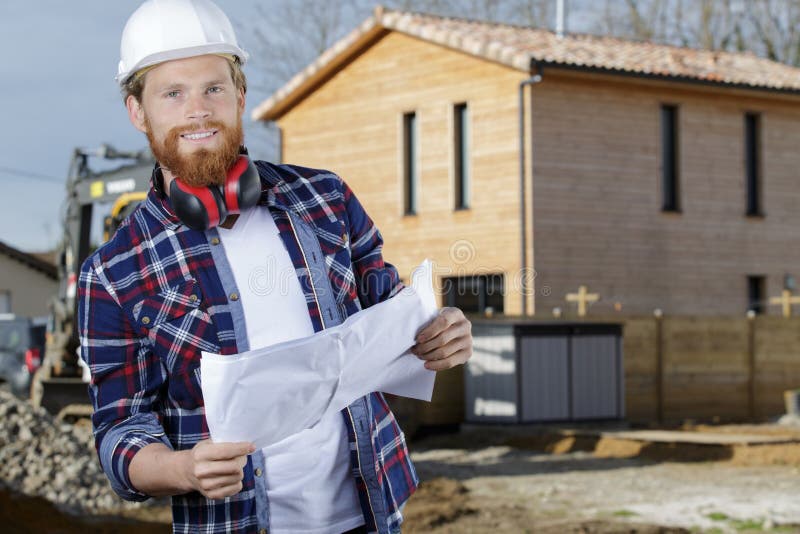 Male Contractor Holding Plans Outside Timber Frame Property Stock Photo ...