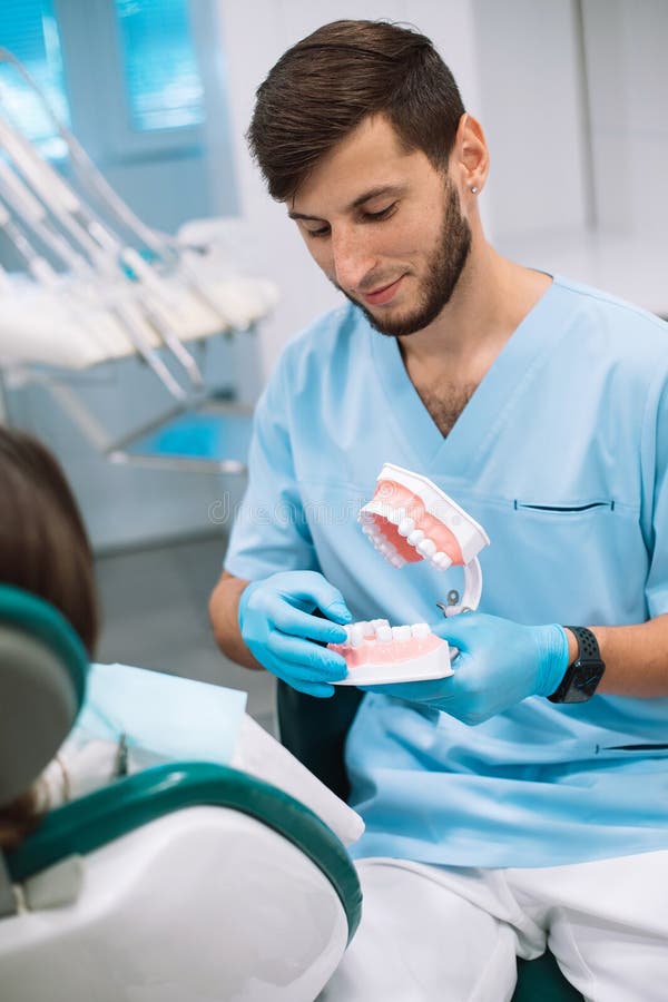 Male Dentist Shows Dentures with a Bracket in Hands To the Patient ...