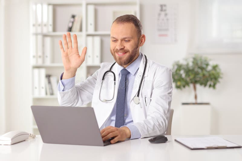 Young Male Doctor Sitting in an Office and Waving at a Laptop Computer ...