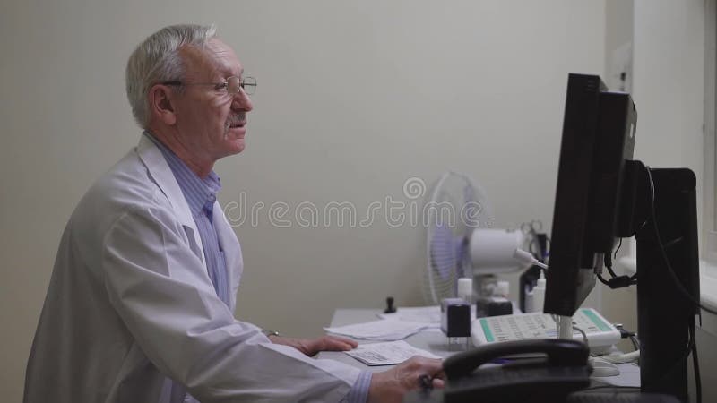 Male Doctor Using Computer. Side View of Senior Male Doctor in Uniform ...