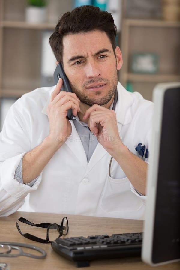 Male Doctor Using Telephone while Working on Computer in Clinic Stock ...
