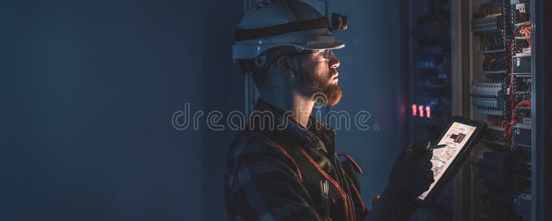 A Male Electrician in Overalls, Focused on Work in Switchboard with ...