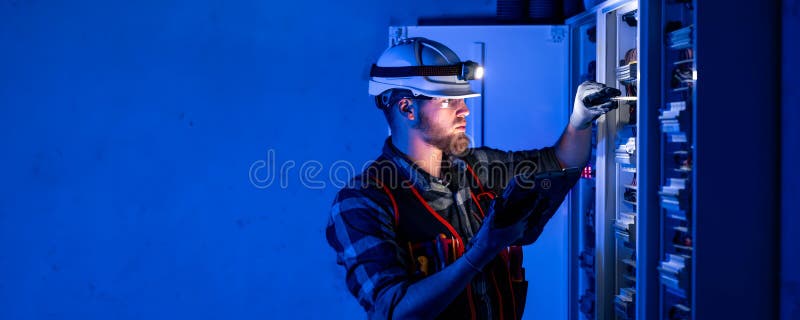 A Male Electrician in Overalls, Focused on Work in Switchboard with ...