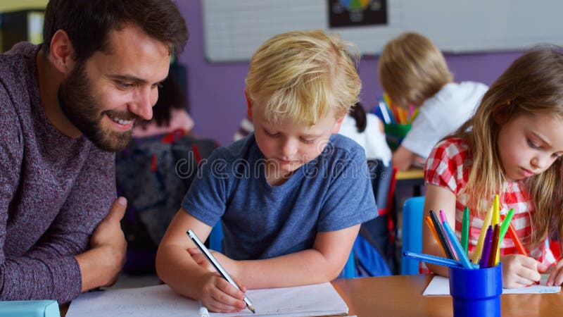 Male Elementary School Teacher Giving Male Pupil One To One Support in ...