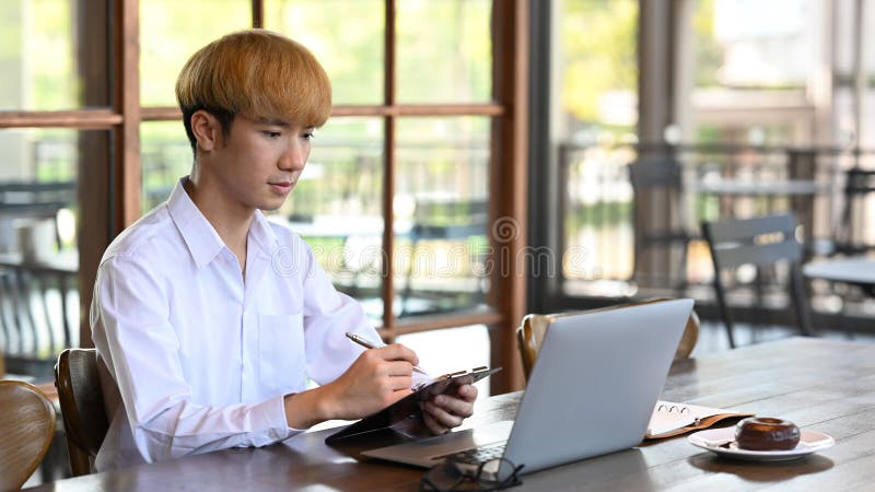Male Employee Reading Information on Laptop and Making Notes on ...