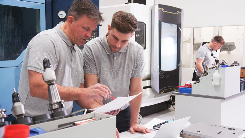 Male Engineer and Apprentice Discussing Plans for Job Whilst Looking at ...