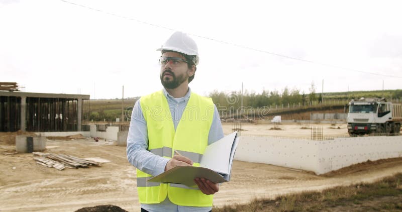 Male Engineer in Uniform and White Helmet Makes Notes in Notebook at ...