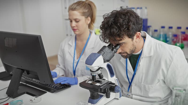 A Male and Female Scientist Examining Samples through a Microscope in a ...