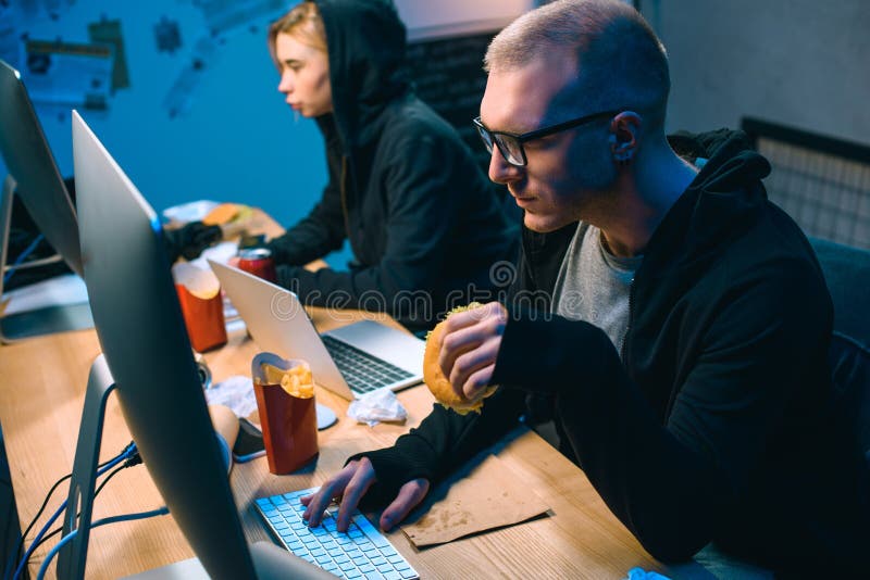 Male Hacker Working on Malware with Accomplice and Eating Stock Photo ...
