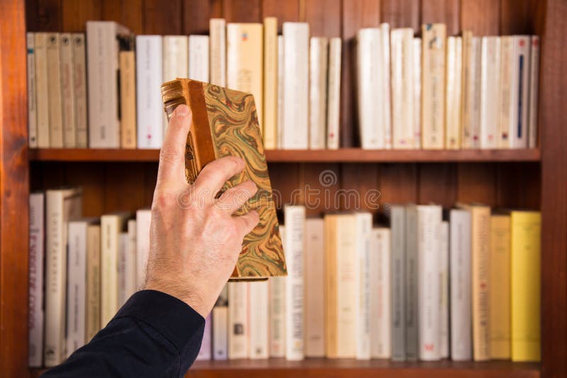 Male Hand Holding a Book in Front of Bookshelves Stock Image - Image of ...
