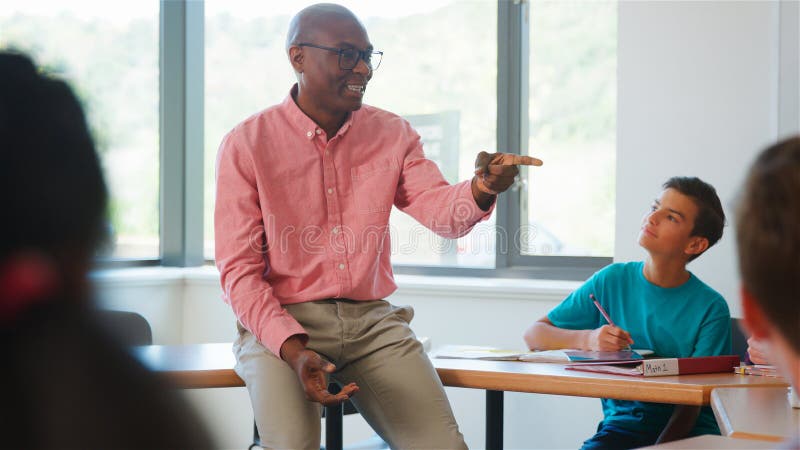 Male High School Tutor Sitting on Desk Teaching Group of Multi-Cultural ...