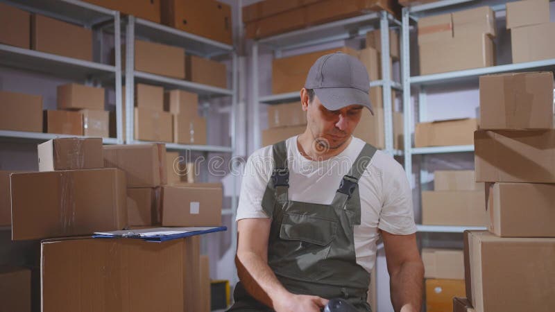 A Male Loader in Uniform Works with Parcels Using a Barcode Scanner in ...