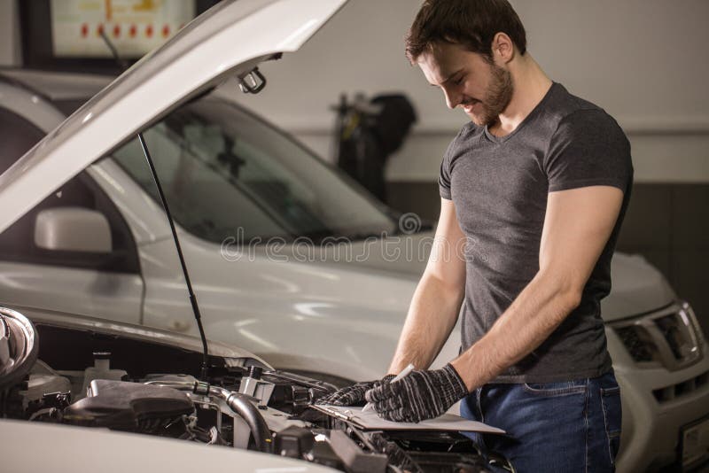 Mechachic Checking on Car Engine and Taking Notes in Clipboard ...