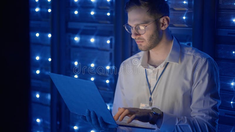 Male Network Engineer Doing a System Check Standing in the Server Room ...