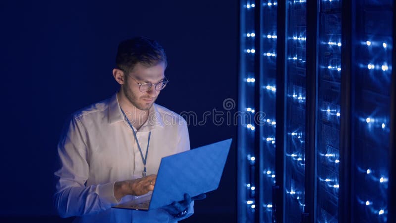 Male Network Engineer Doing a System Check Standing in the Server Room ...