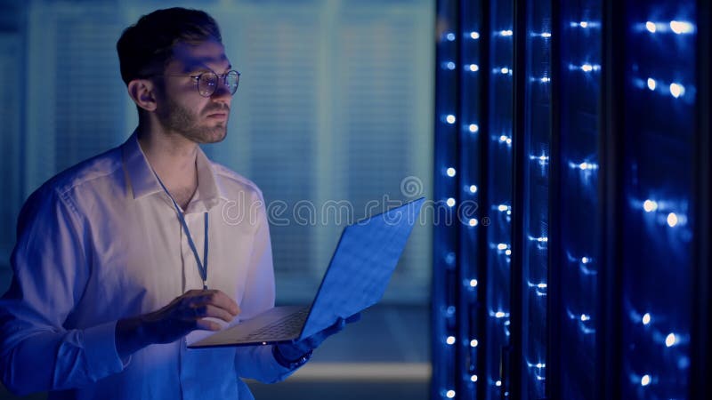 Male Network Engineer Doing a System Check Standing in the Server Room ...