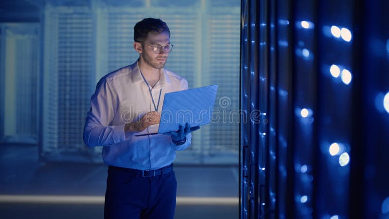 Male Network Engineer Doing a System Check Standing in the Server Room ...