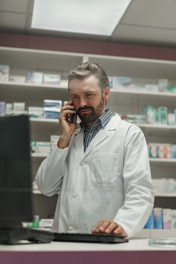 Male Pharmacist Wearing Lab Coat Working on Computer in Drugstore and ...