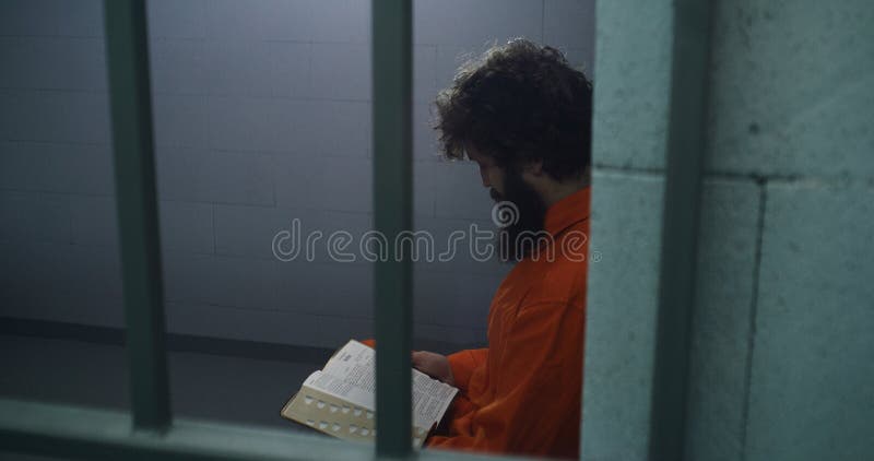 Male Prisoner in Orange Uniform Sits on the Bed, Reads Bible Stock ... Male Prisoner in Orange Uniform Sits on the Bed, Reads Bible Stock ...