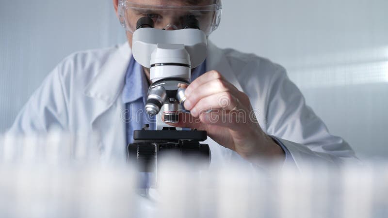 Male Scientist Wearing Lab Coat and Protective Glasses Using Microscope ...