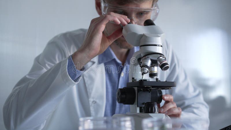Male Scientist Wearing Lab Coat and Protective Glasses Using Microscope ...