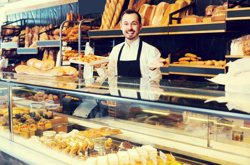Male Shop Assistant Demonstrating Fresh Delicious Pastry In Bake Stock