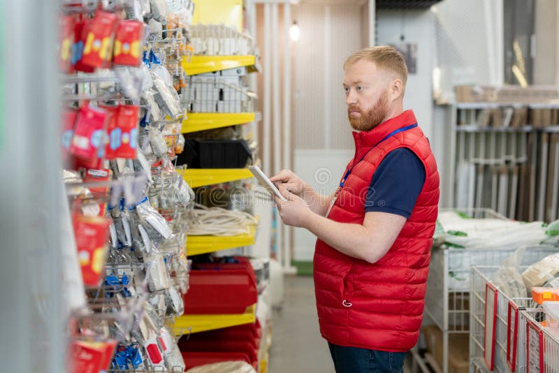 Male Shop Assistant in Red Uniform Using Tablet while Checking Goods in ...