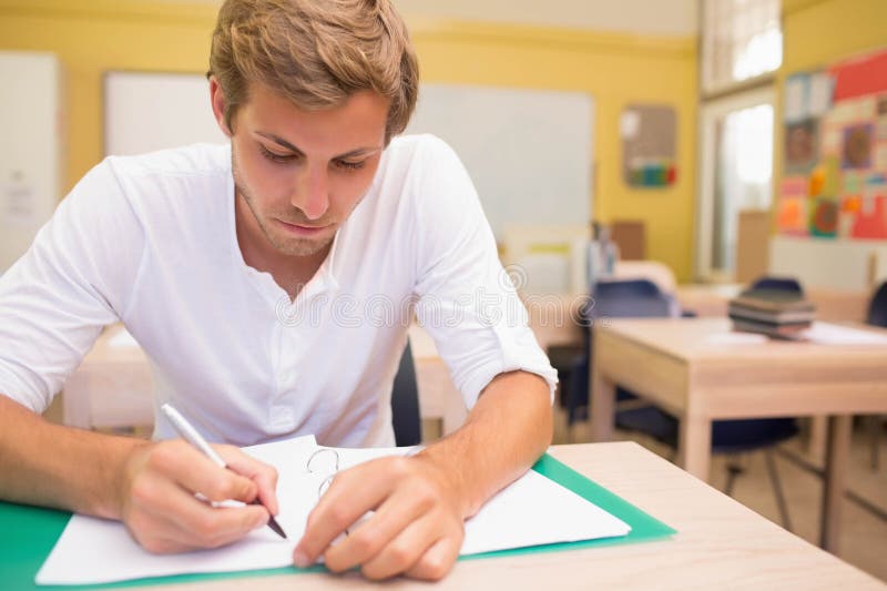 Male Student Leaning Forward Writing in Binder on Green Folder at ...