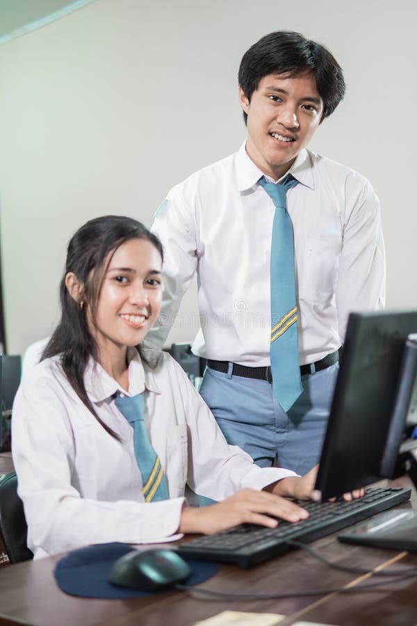 A Male Student Stands Smiling at the Camera while a Female Student Uses ...