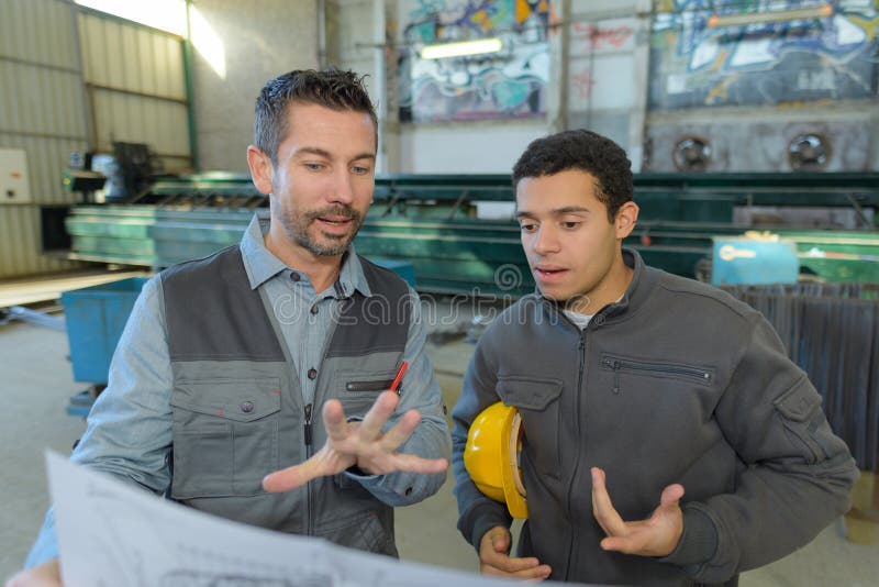 Male Supervisor with Workers Discussing Over Blueprints in Industry ...