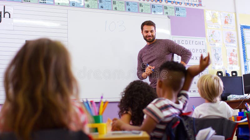 Male Teacher Standing at Whiteboard Teaching Maths Lesson To Elementary ...