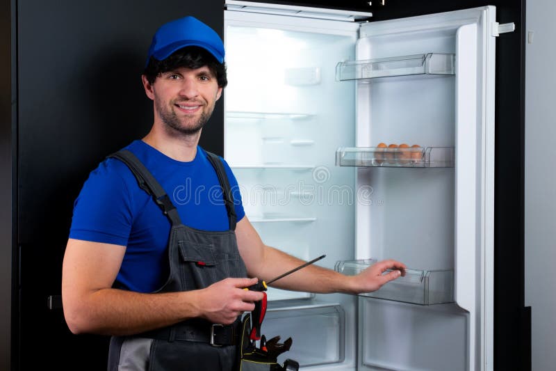 Male Technician in Uniform Repairs a Broken Refrigerator in the Kitchen ...